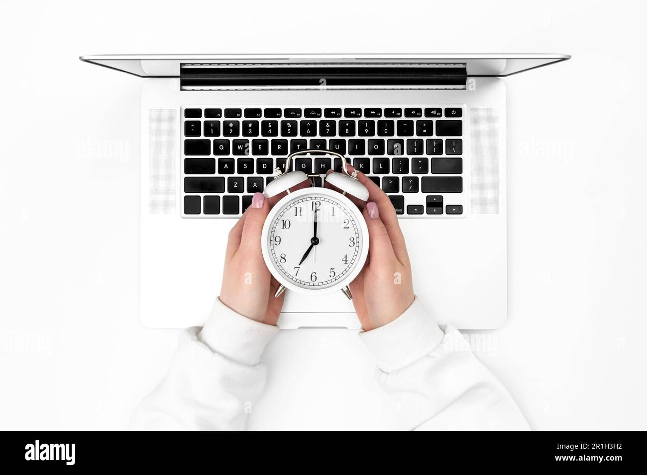 Alarm clock in female hands and a laptop on a white background, top ...