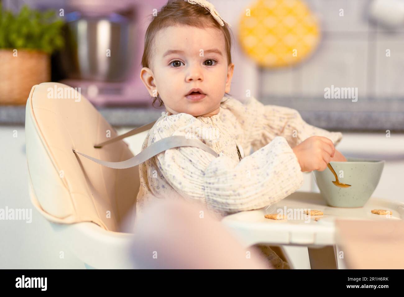 Little baby girl sitting in a highchair eating by herself with a spoon ...