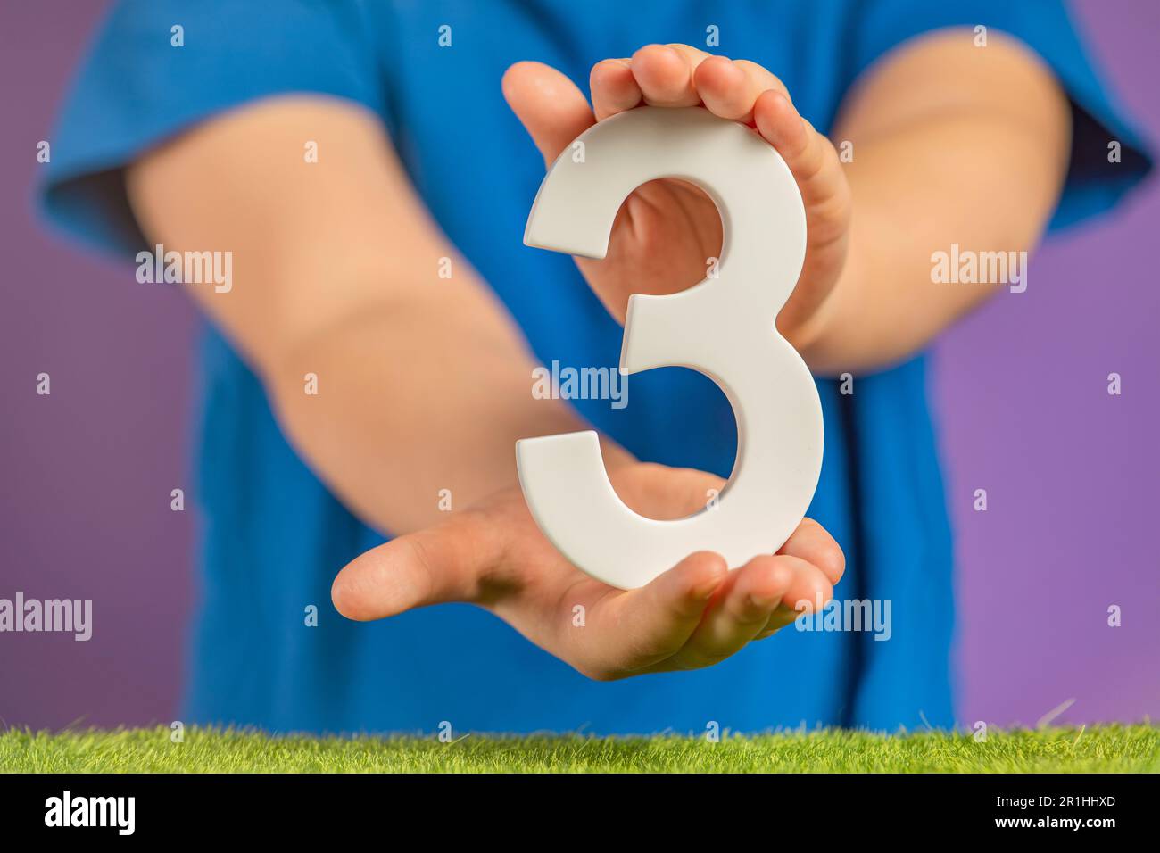 Number 3 in hand. Hand holding white number three over green grass and ...