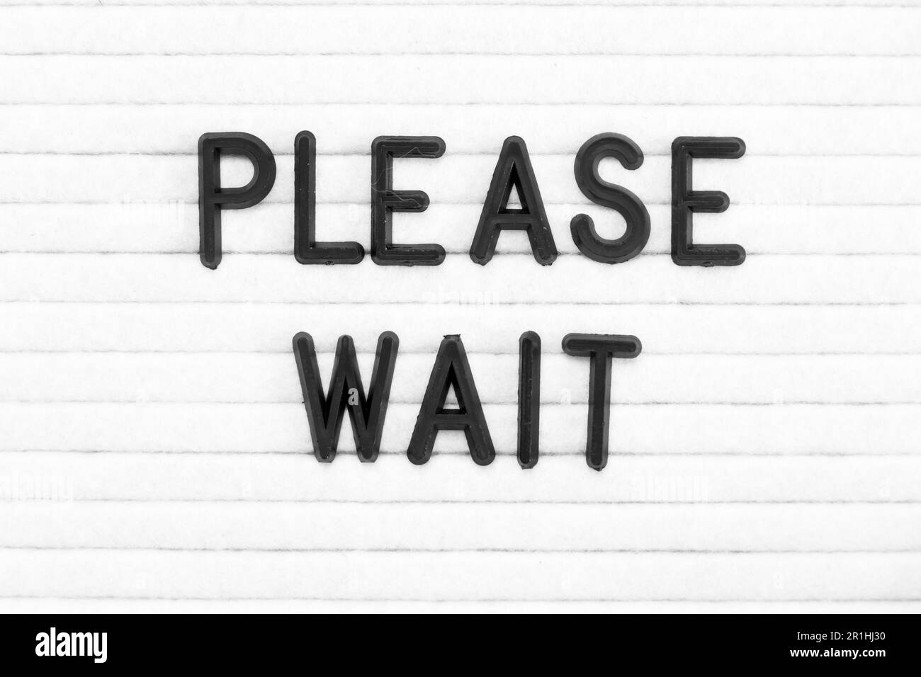 Black color letter in word please wait on white felt board background ...