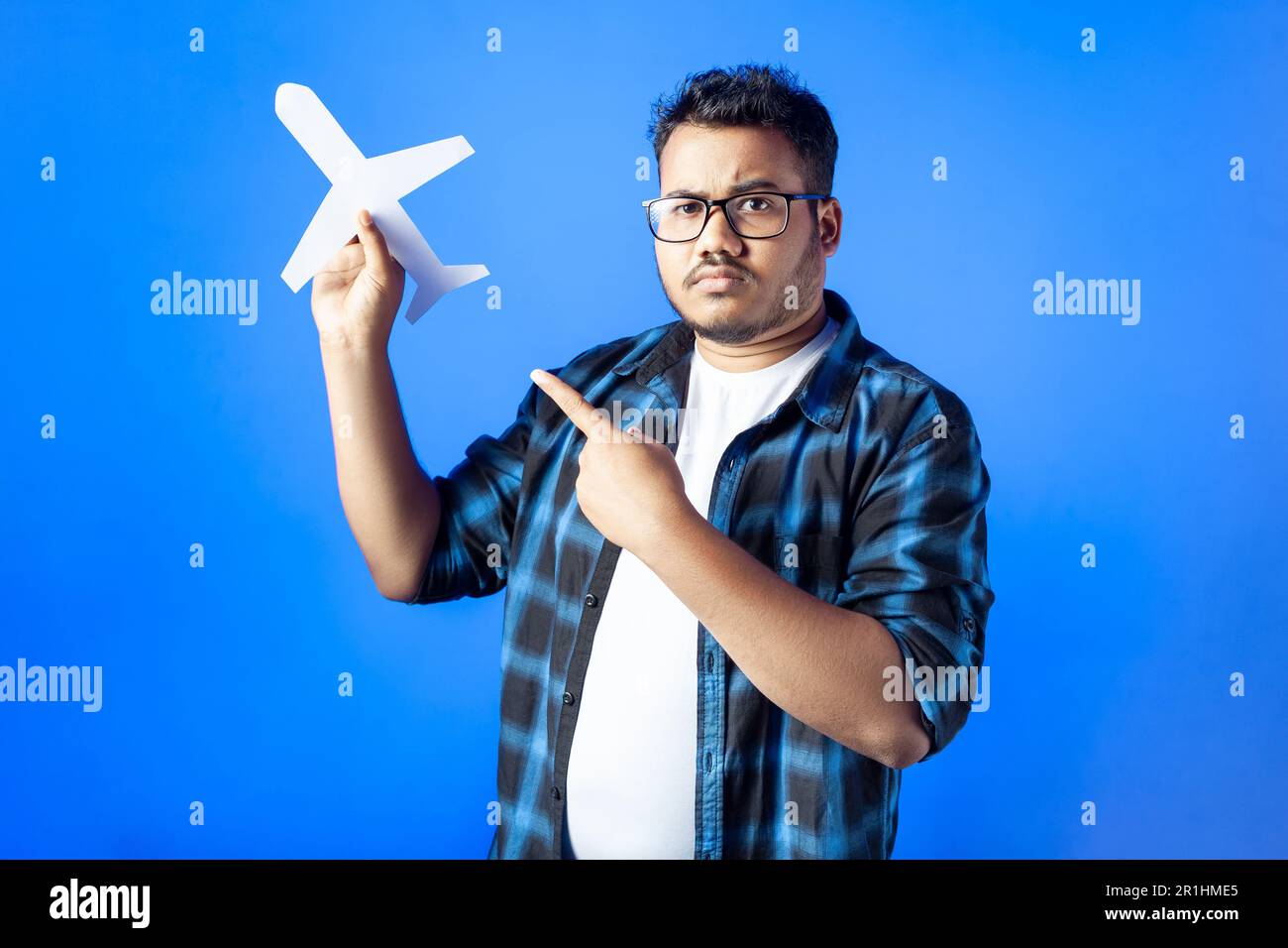 In blue background an Indian young man looking serious, holding paper ...