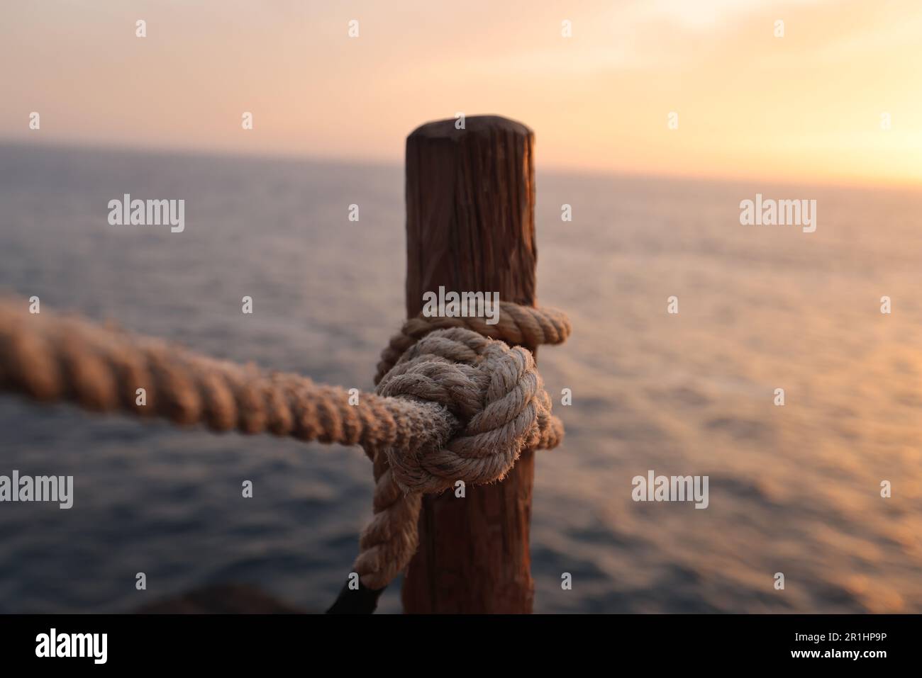A close-up shot of a rope tied around a wooden post on the sandy beach ...