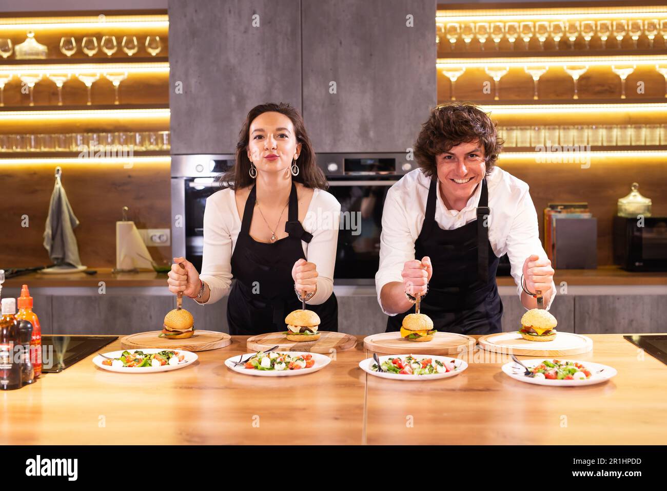 Funny chef and his colleague standing at kitchen and looking at camera ...