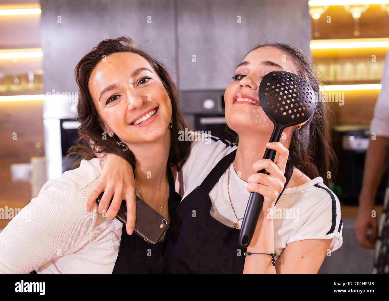 Two funny female chef in uniform holding kitchenware while smiling and ...