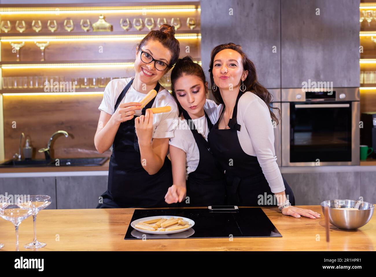 Three funny female chef in uniform holding cookies while smiling and ...