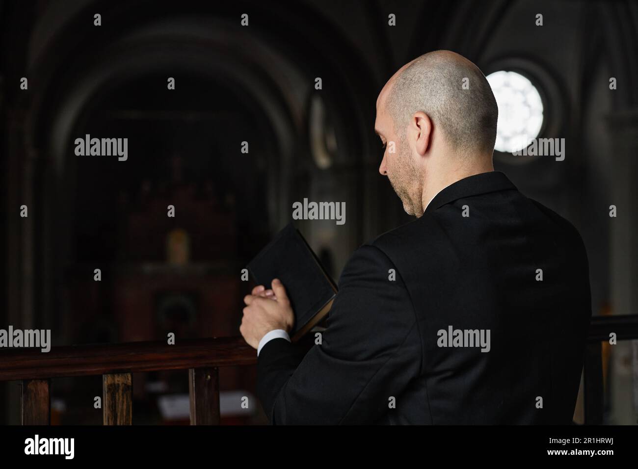 Rear view of pastor in black suit standing with Bible and praying in ...