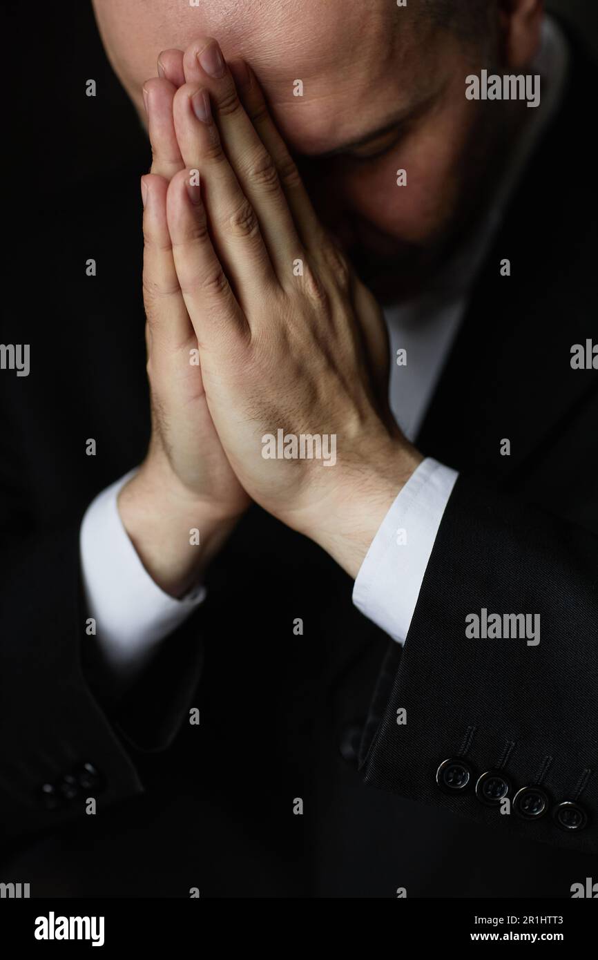 Vertical image of mature man in black suit praying with his eyes closed ...