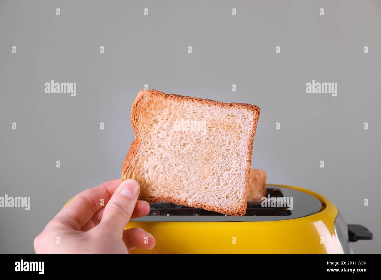 Woman taking off roasted bread from toaster against grey background ...