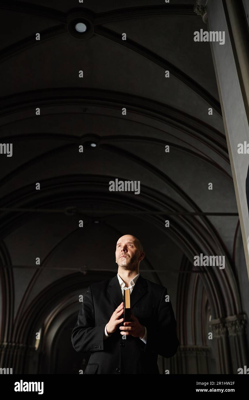 Vertical image of mature man with Bible standing in old church with ...