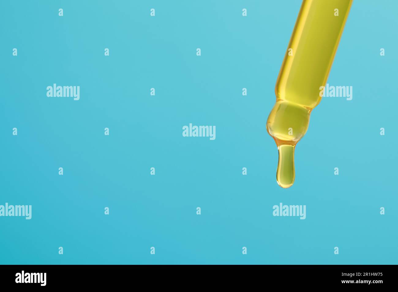 Dripping yellow serum from pipette on light blue background, closeup ...