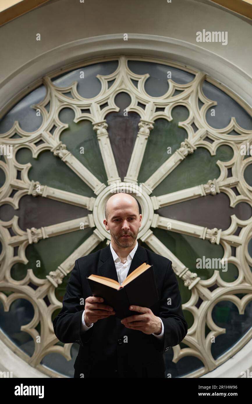Vertical image of serious mature pastor in suit reading Bible standing ...