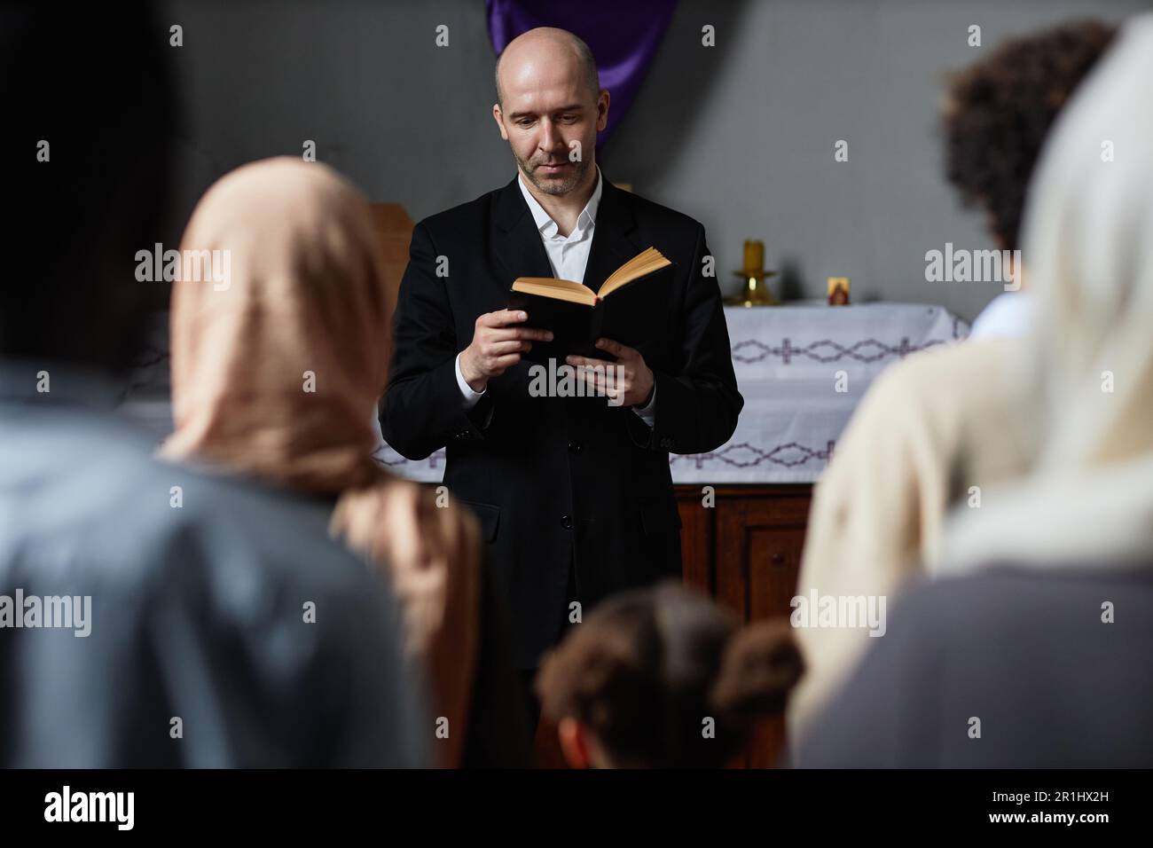 Mature preacher in black suit reading Bible for believers standing near ...