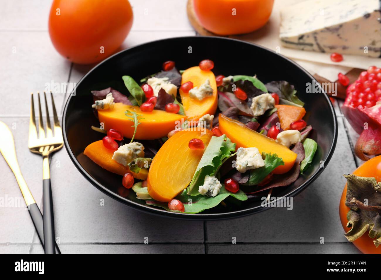 Delicious persimmon salad and fork on tiled surface Stock Photo - Alamy