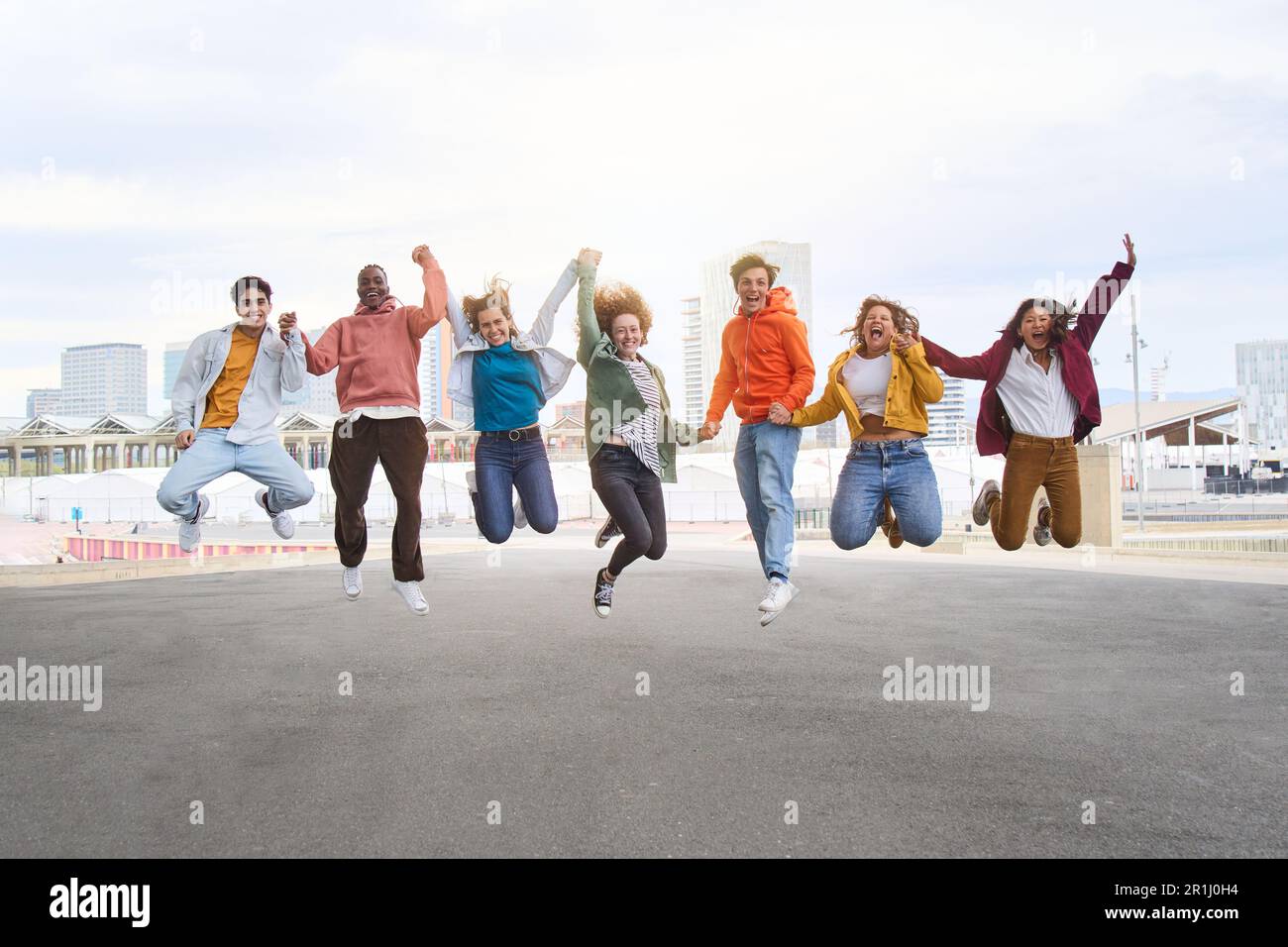 Excited multicultural friends jumping holding hands in city street ...