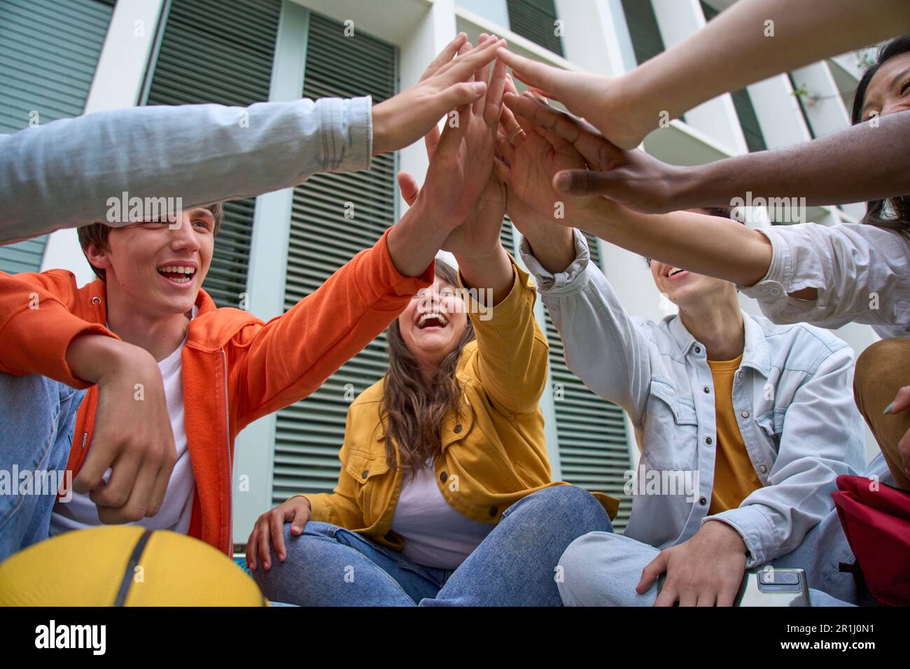 Group of cheerful young friends joining hands in circle sitting outside ...