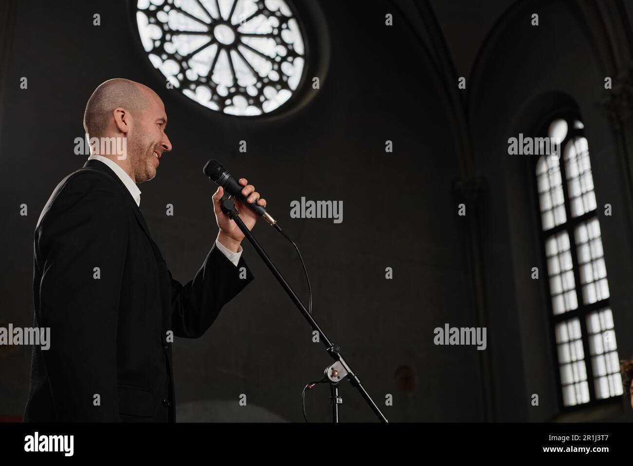 Mature pastor in black suit speaking prayer in microphone while ...