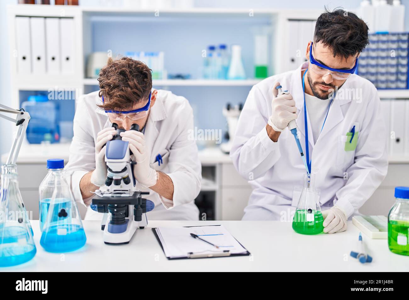 Young couple wearing scientist uniform using microscope and pipette at ...