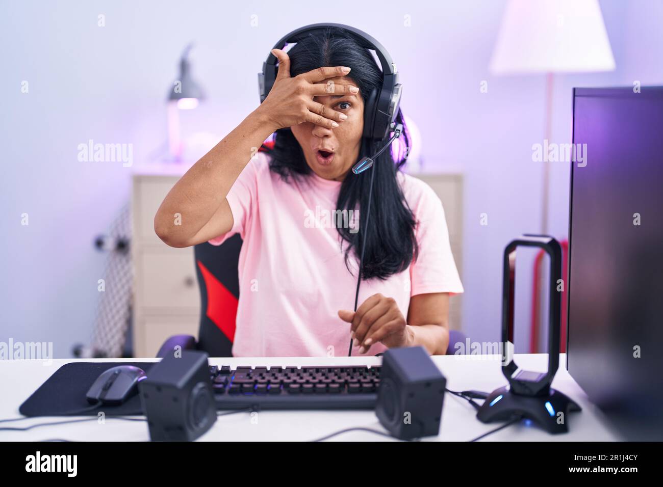 Mature hispanic woman playing video games at home peeking in shock ...