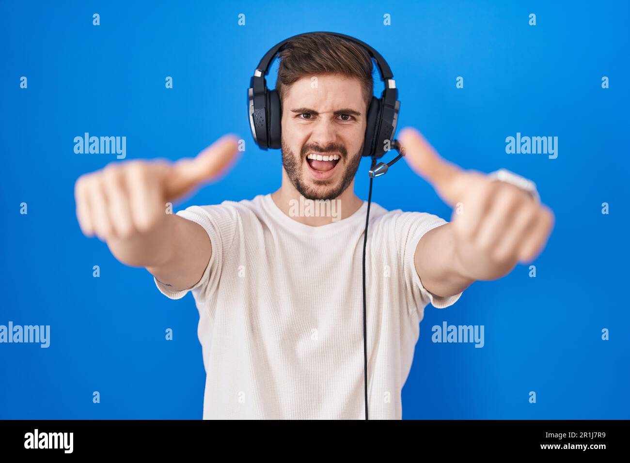 Hispanic man with beard listening to music wearing headphones approving ...