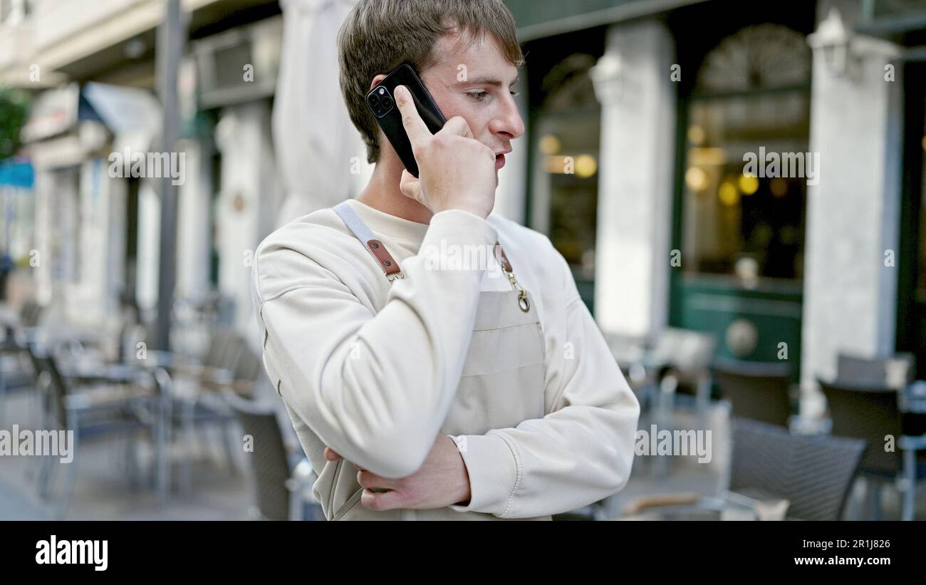 Young caucasian man waiter talking on smartphone at coffee shop terrace ...