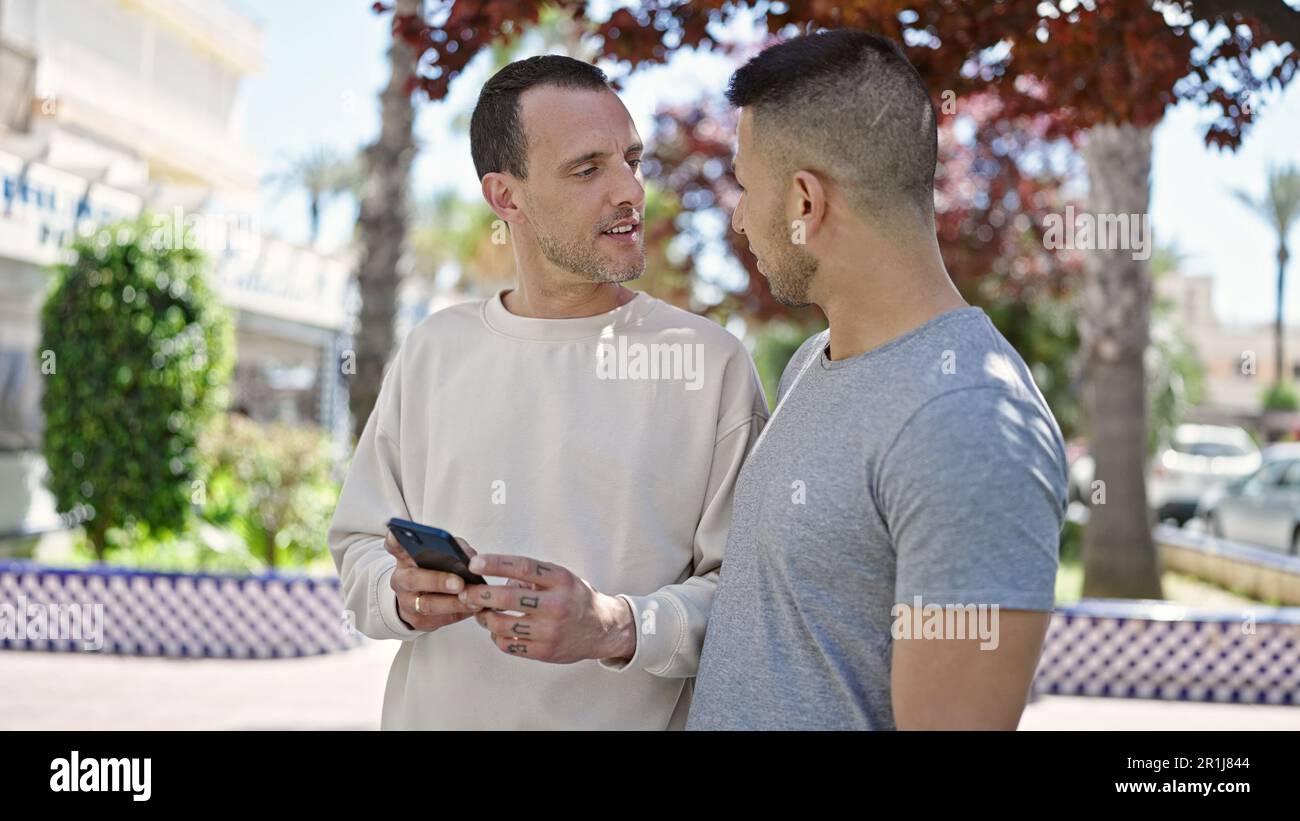 Two men couple using smartphone at park Stock Photo - Alamy