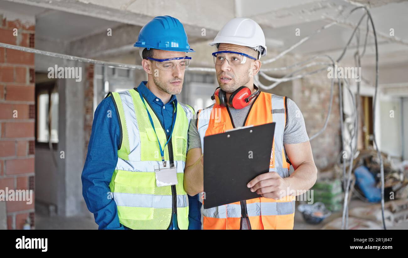 Two men builders reading document speaking at construction site Stock ...