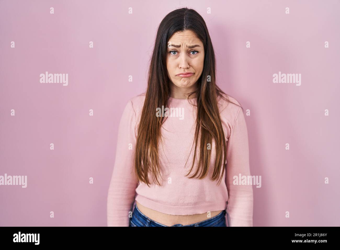 Young brunette woman standing over pink background depressed and worry ...