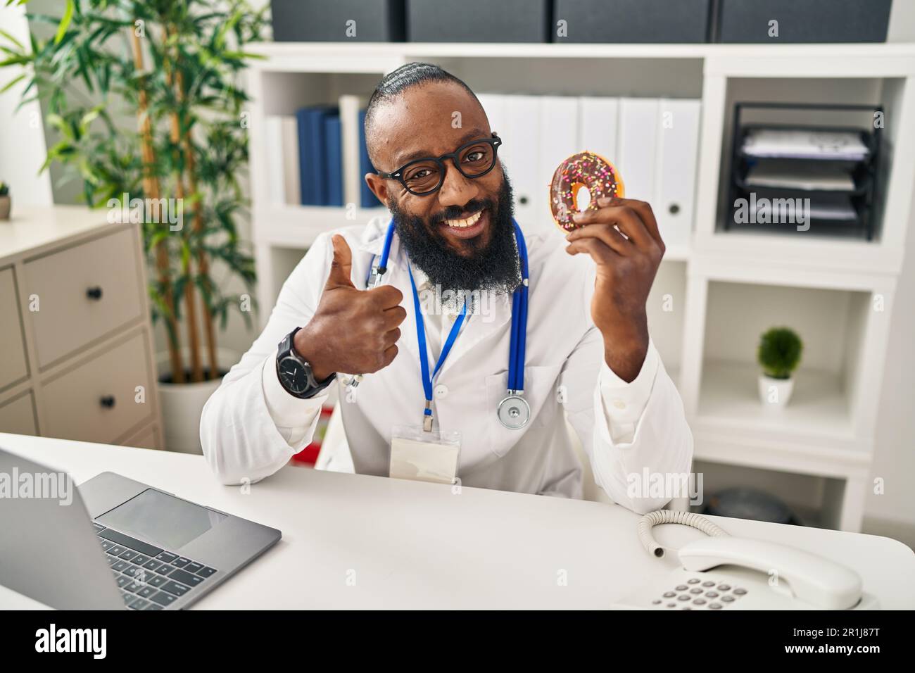African american man working at dietitian clinic holding doughnut ...