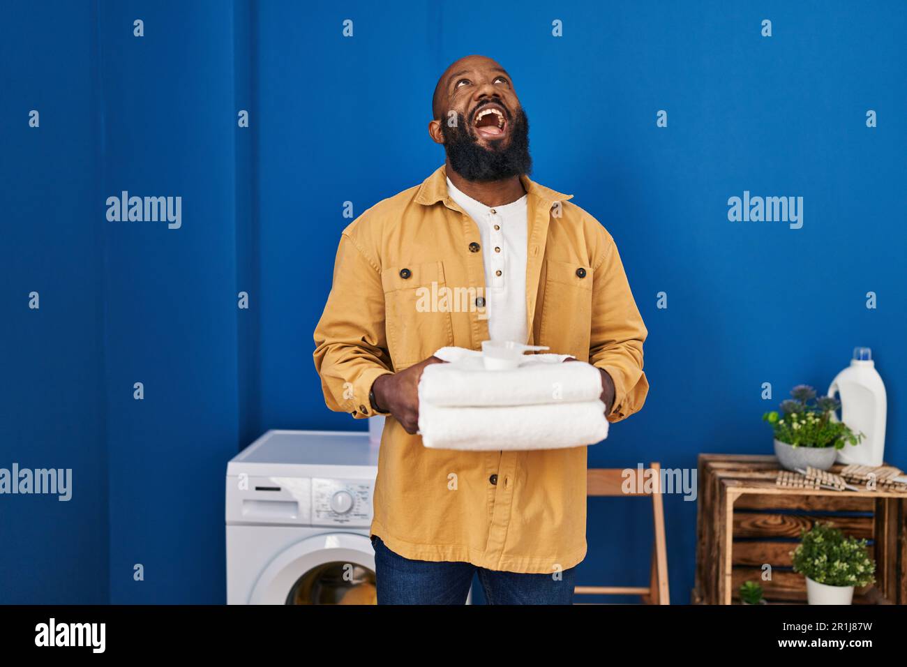 African american man holding clean towels at laundry room angry and mad ...