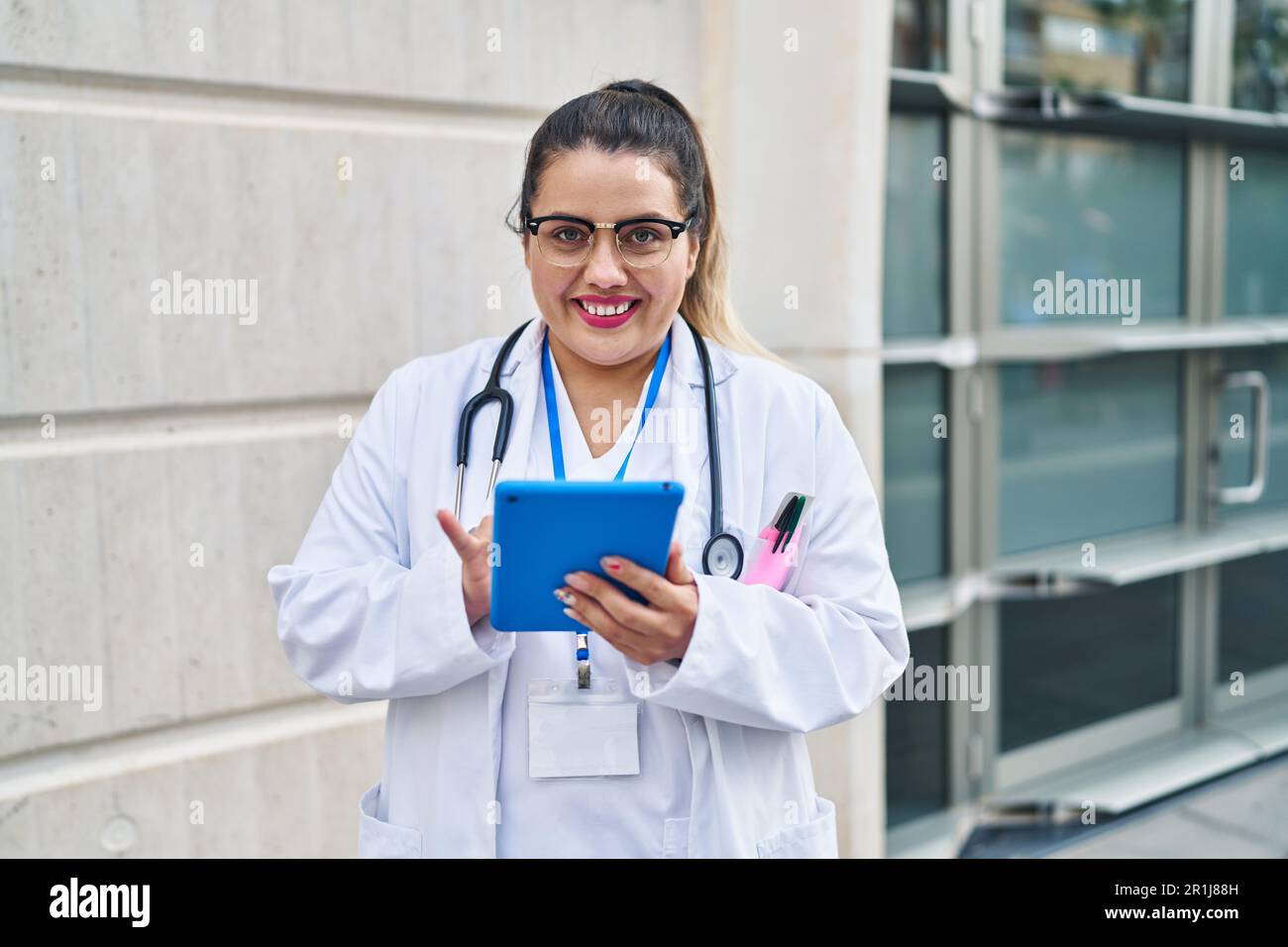 Young beautiful plus size woman doctor smiling confident using touchpad ...