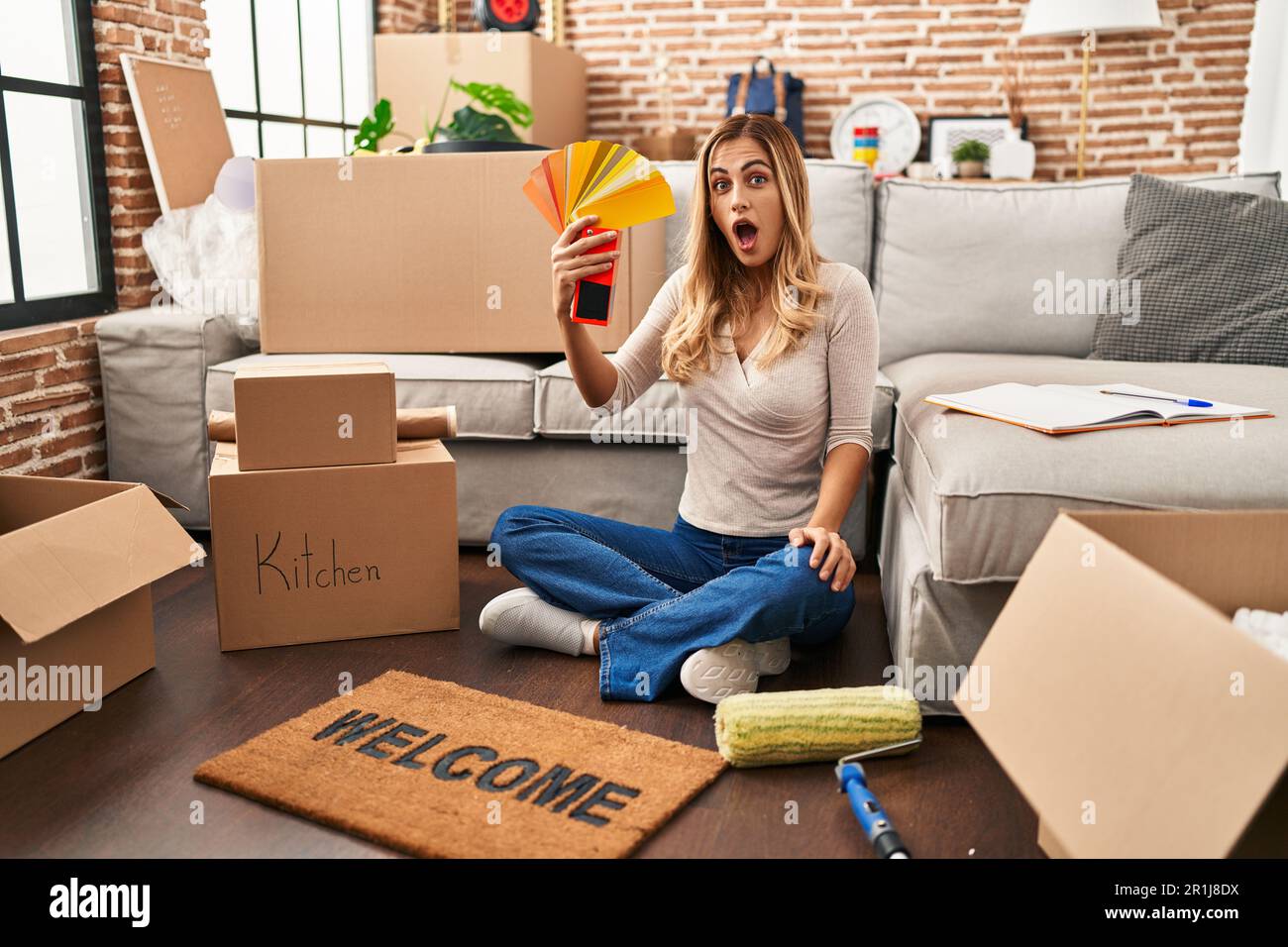 Young blonde woman choosing paint color at new home scared and amazed ...