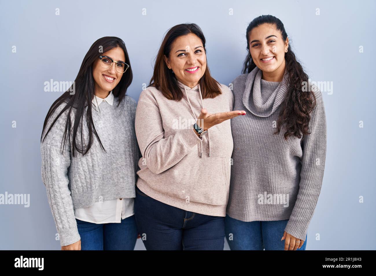 Mother and two daughters standing over blue background pointing aside ...
