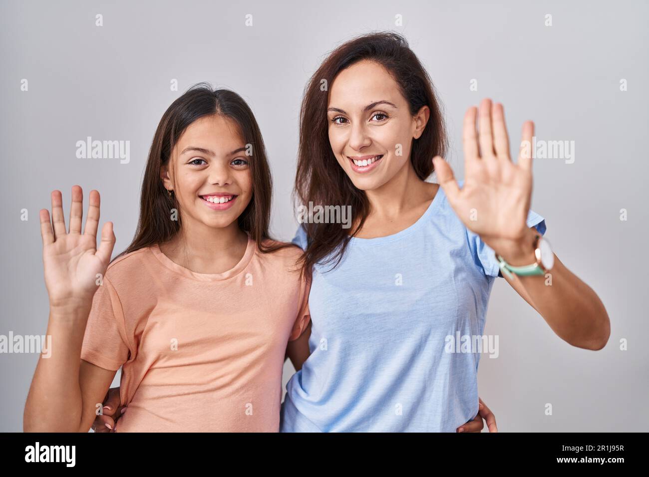Young mother and daughter standing over white background waiving saying ...