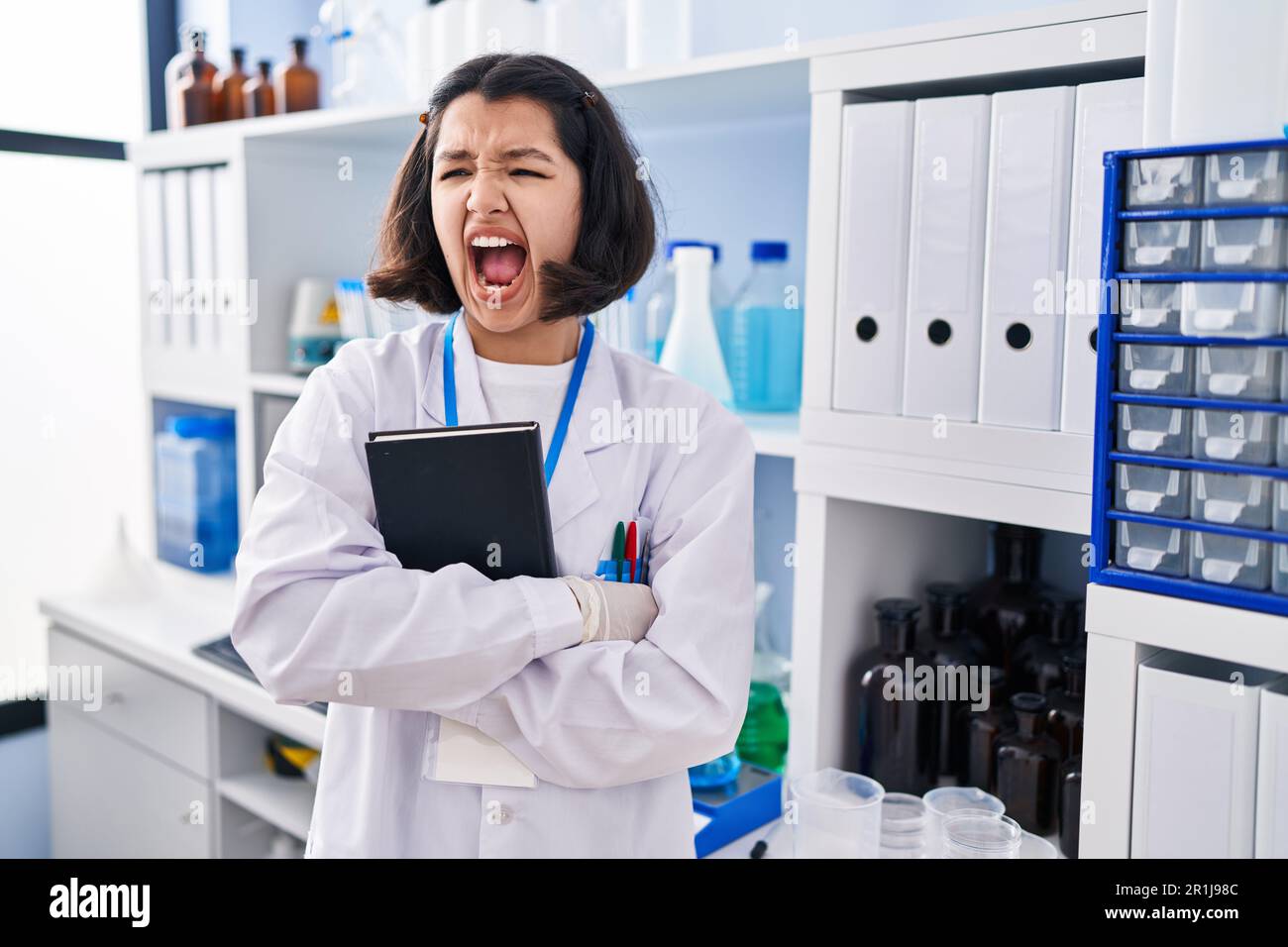 Young hispanic woman working at scientist laboratory angry and mad ...