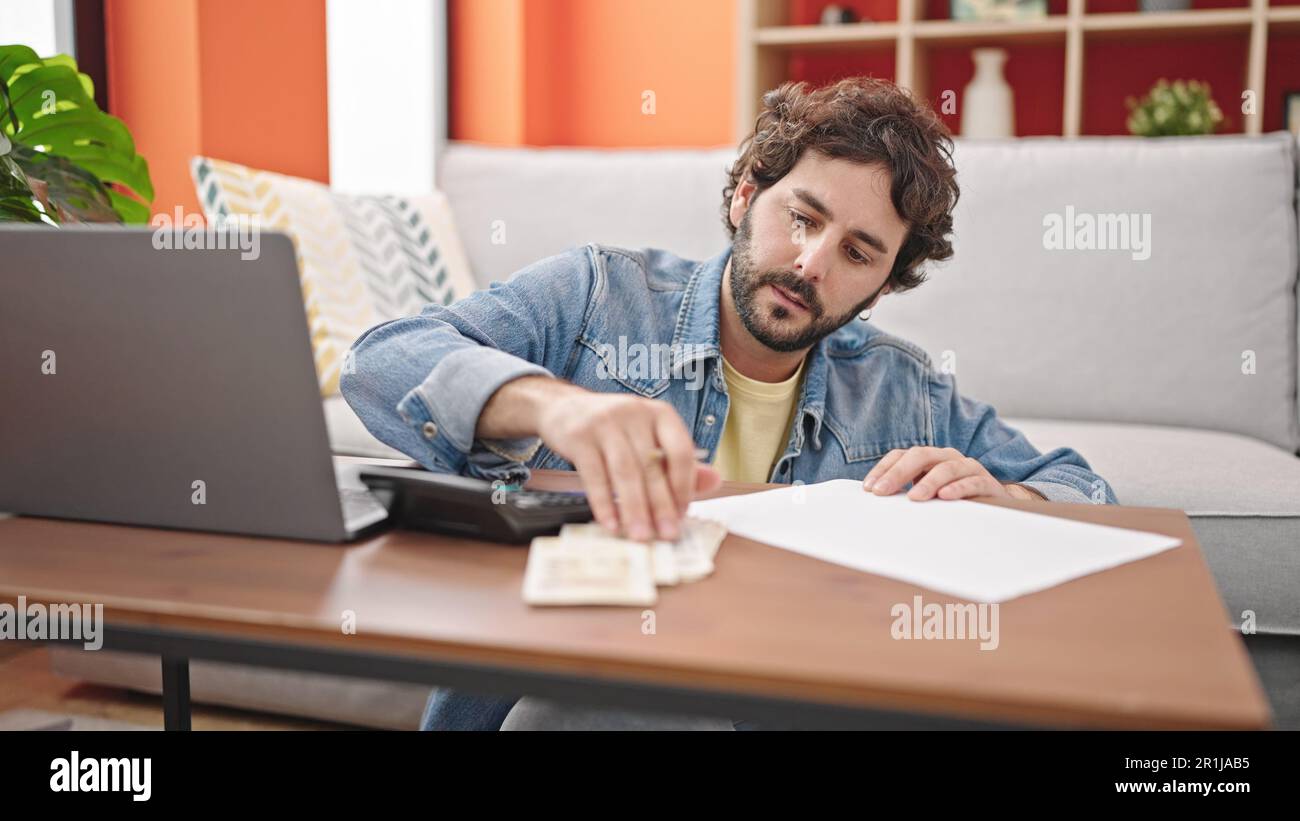 Young hispanic man using laptop and calculator counting denmark krone ...