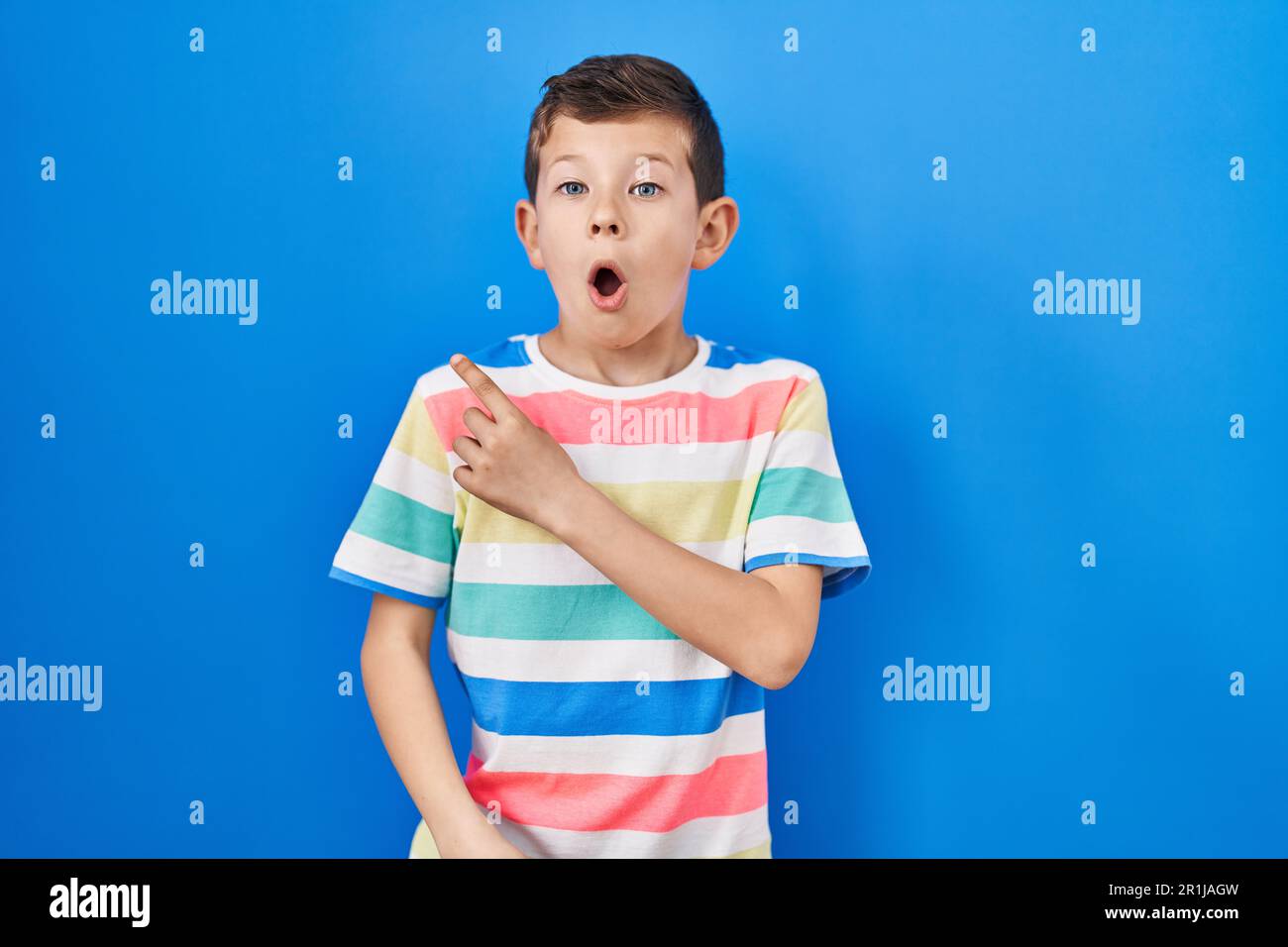 Young caucasian kid standing over blue background surprised pointing ...