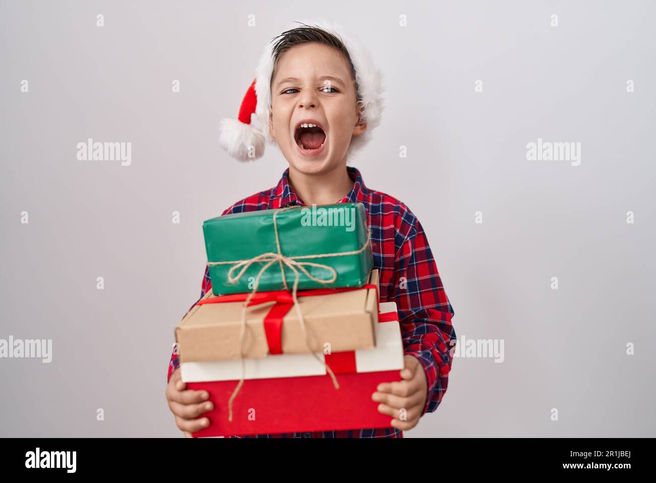 Little hispanic boy wearing christmas hat holding presents angry and ...