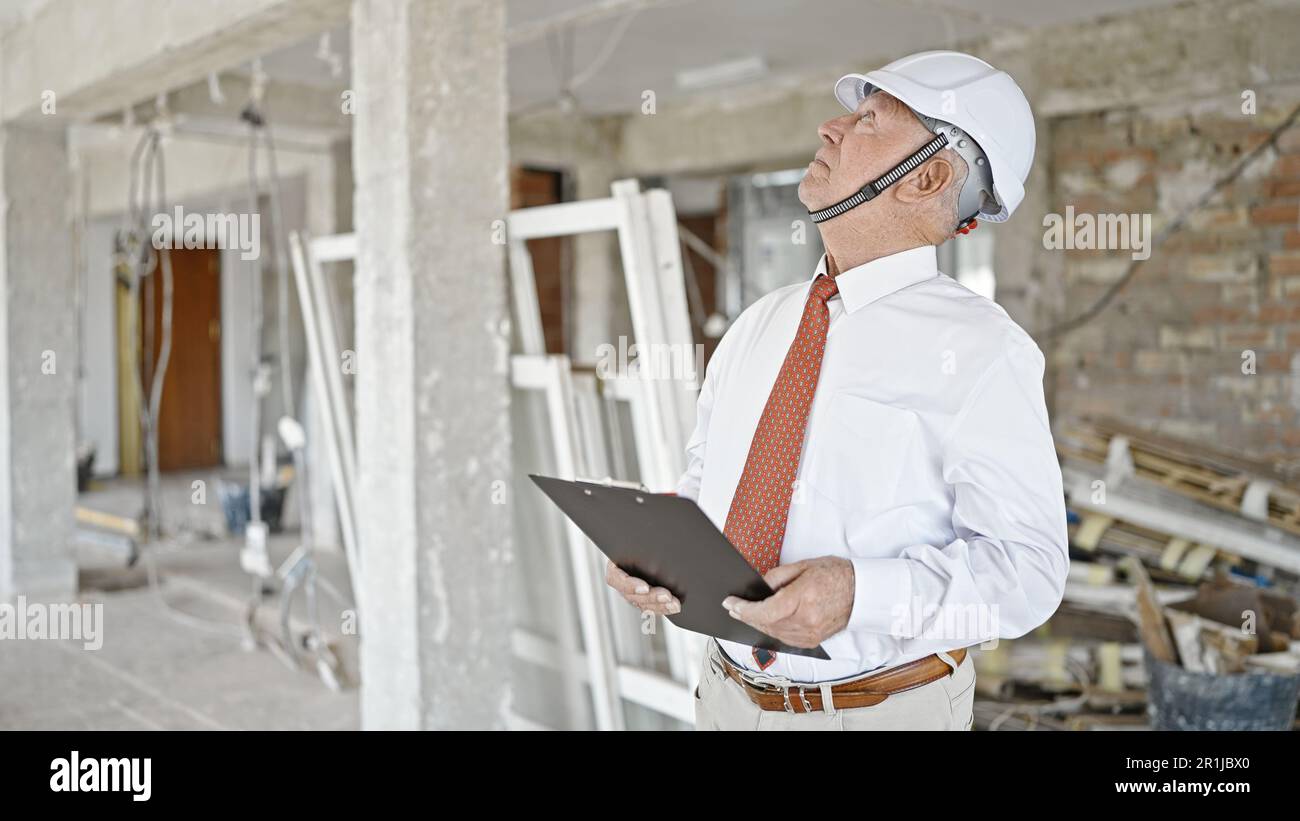 Senior grey-haired man architect holding clipboard looking around at ...