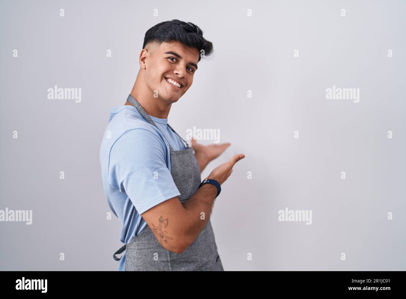 Hispanic young man wearing apron over white background inviting to ...