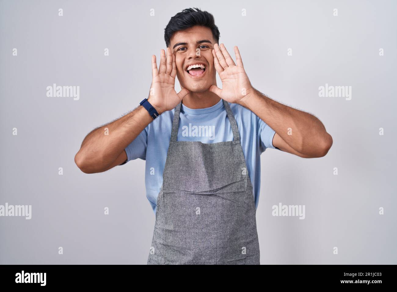 Hispanic young man wearing apron over white background smiling cheerful ...