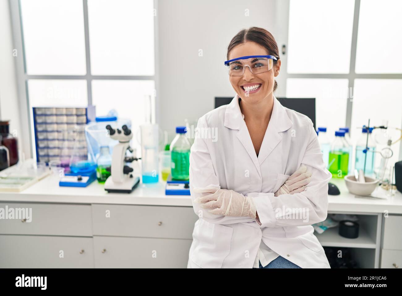 Young beautiful hispanic woman scientist smiling confident sitting with arms crossed gesture at ...