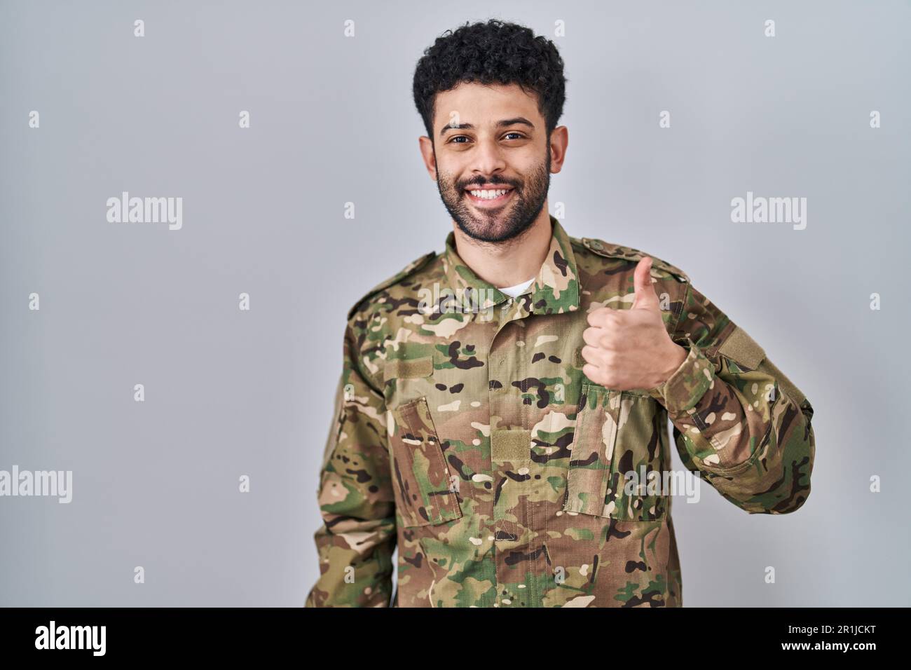 Arab man wearing camouflage army uniform doing happy thumbs up gesture ...