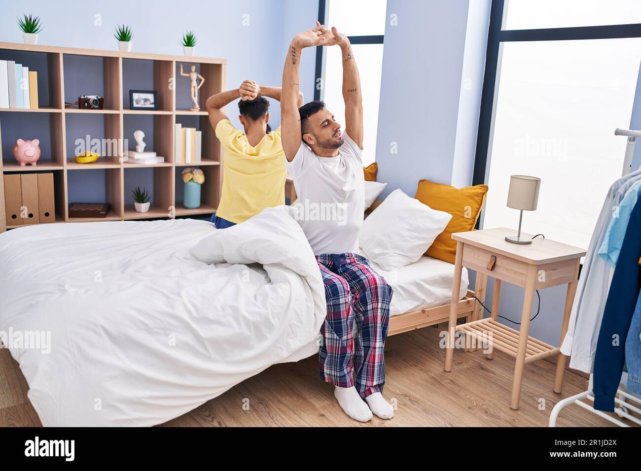 Two man couple waking up stretching arms sitting on bed at bedroom ...