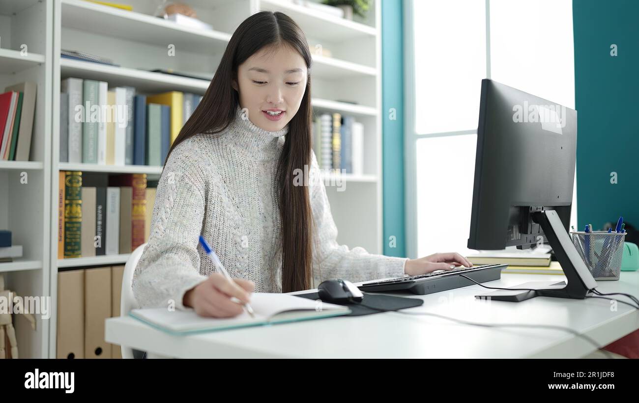Young chinese woman student using computer writing on notebook at ...