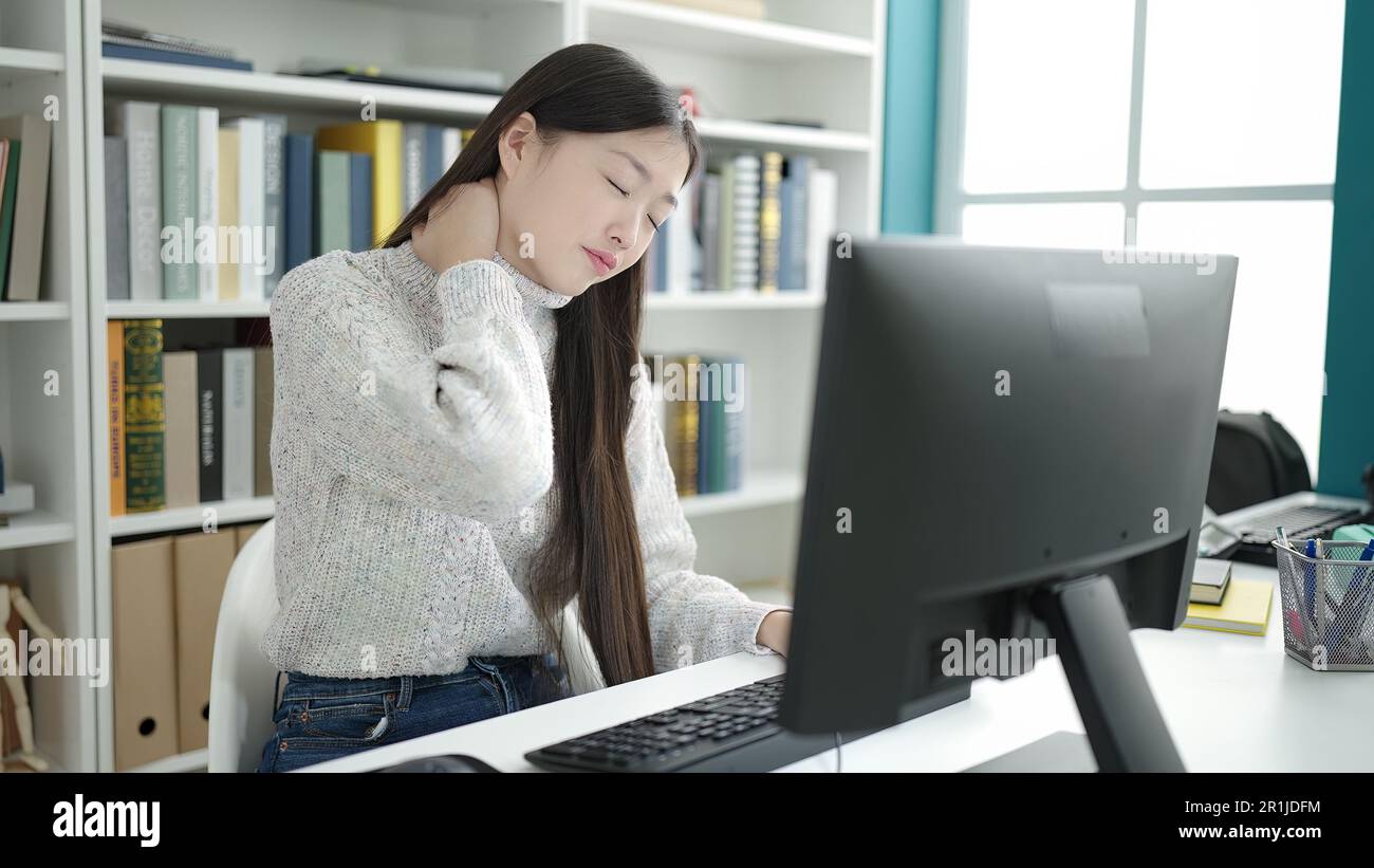 Young chinese woman student using computer stressed at library ...