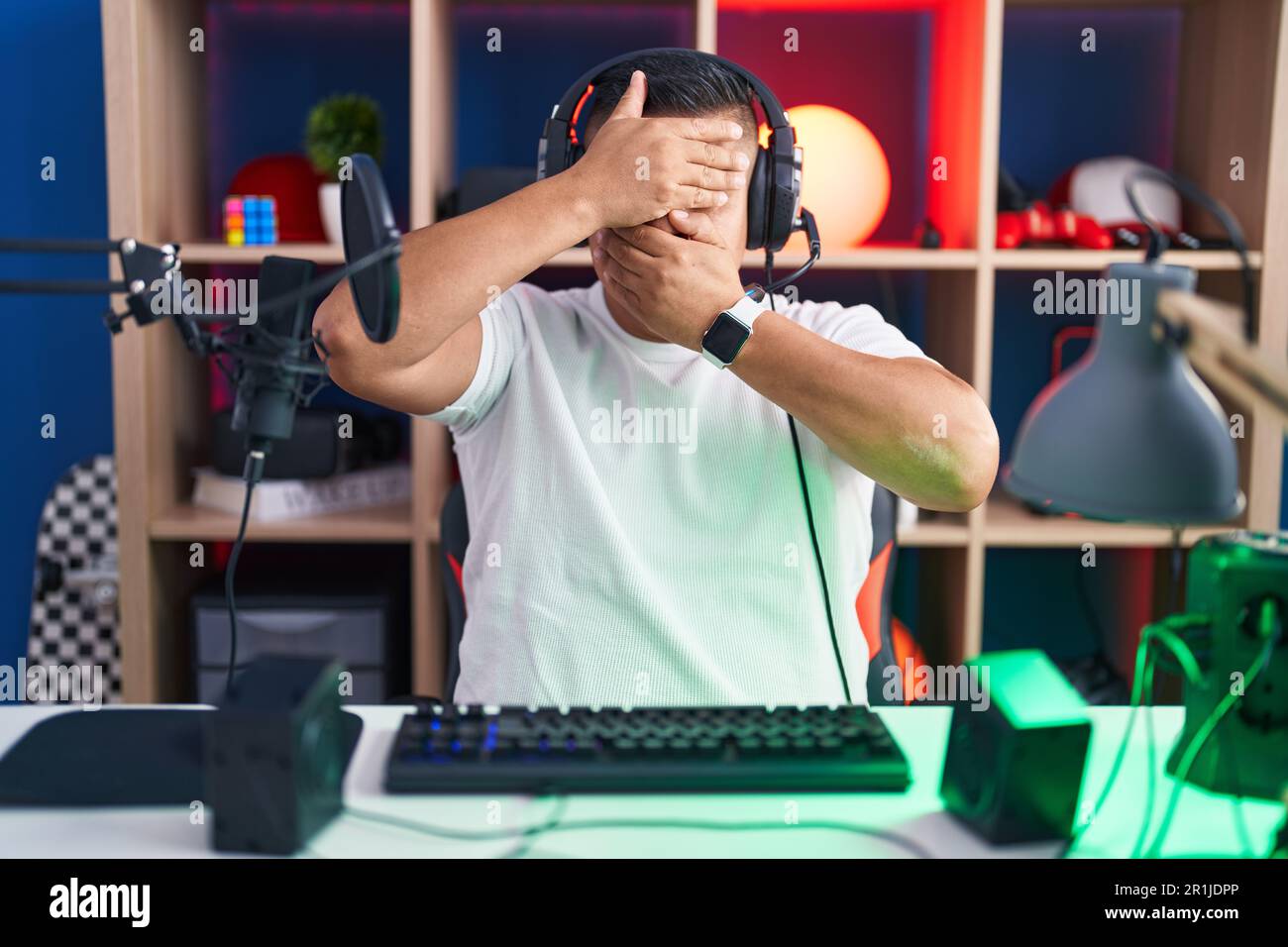 Young hispanic man playing video games covering eyes and mouth with ...