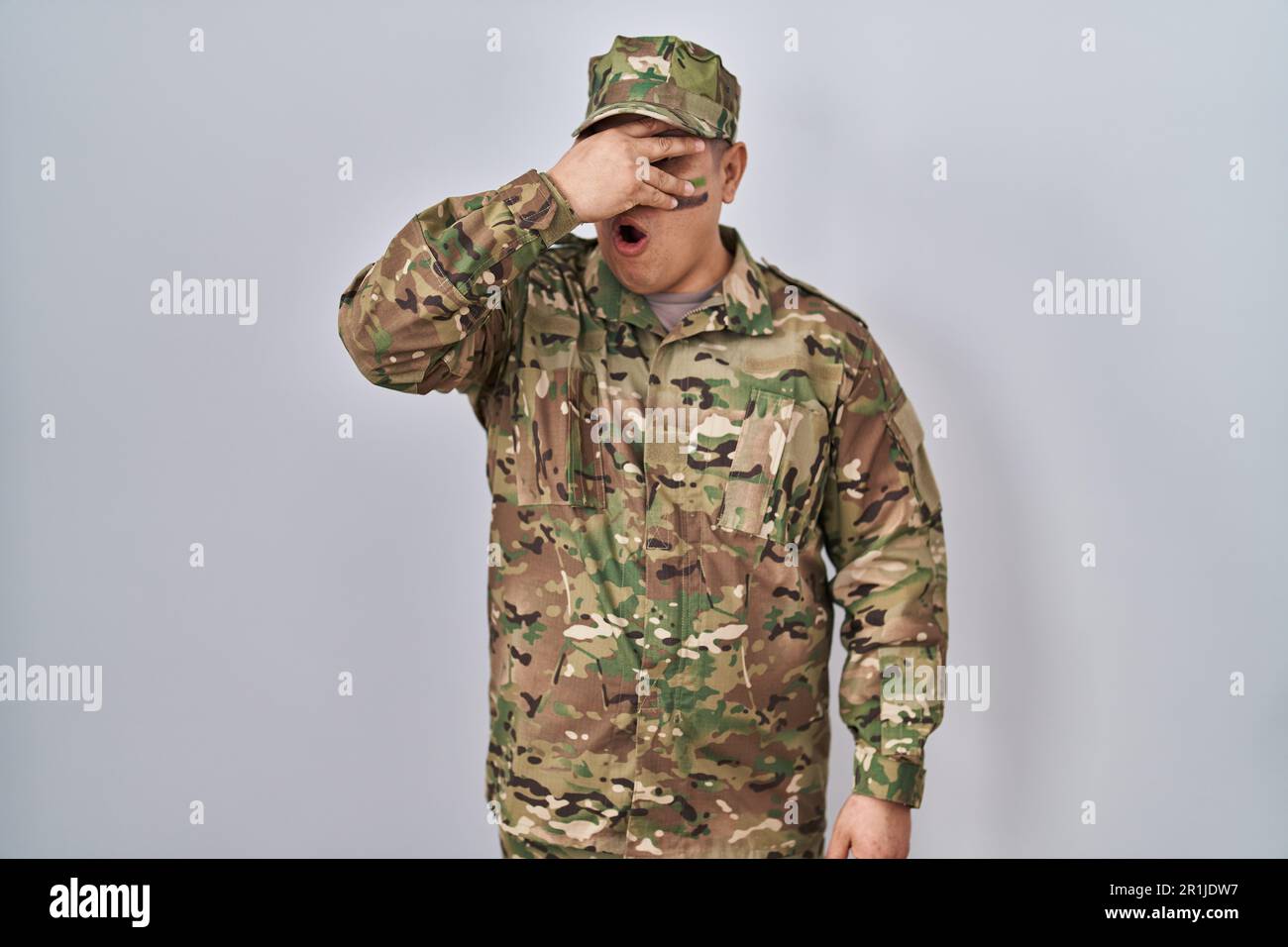 Hispanic young man wearing camouflage army uniform peeking in shock ...
