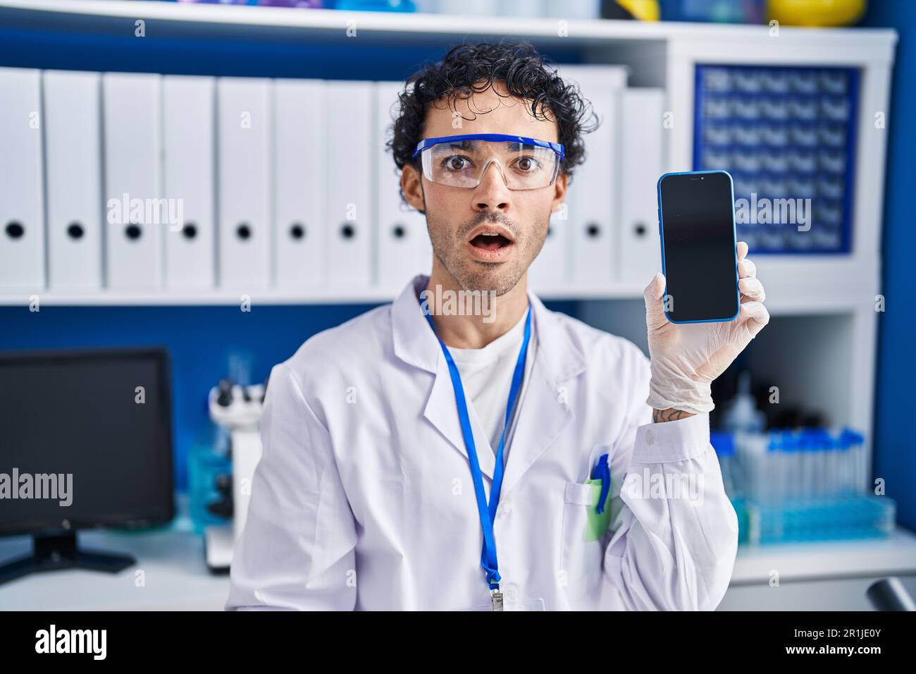 Hispanic man working at scientist laboratory showing smartphone screen ...