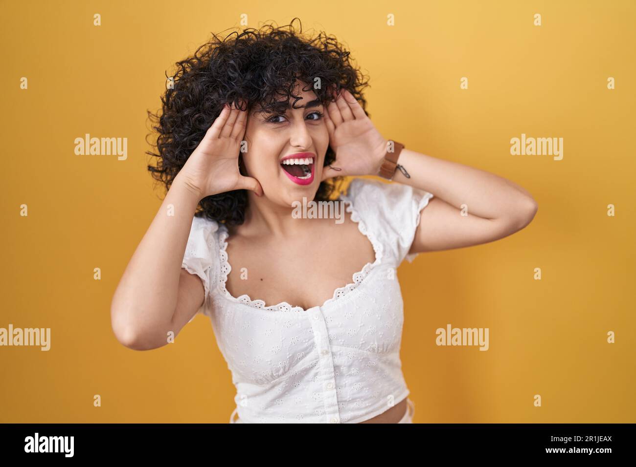 Young brunette woman with curly hair standing over yellow background ...