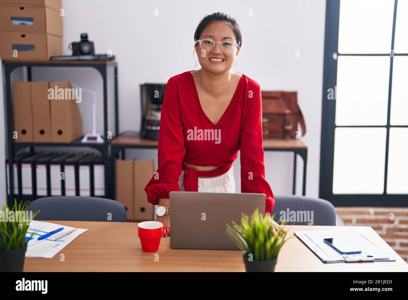Young chinese woman business worker smiling confident standing by desk ...